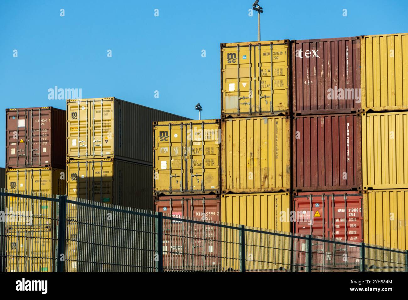 Metal shipping containers stacked high behind a chain link fence at a ...