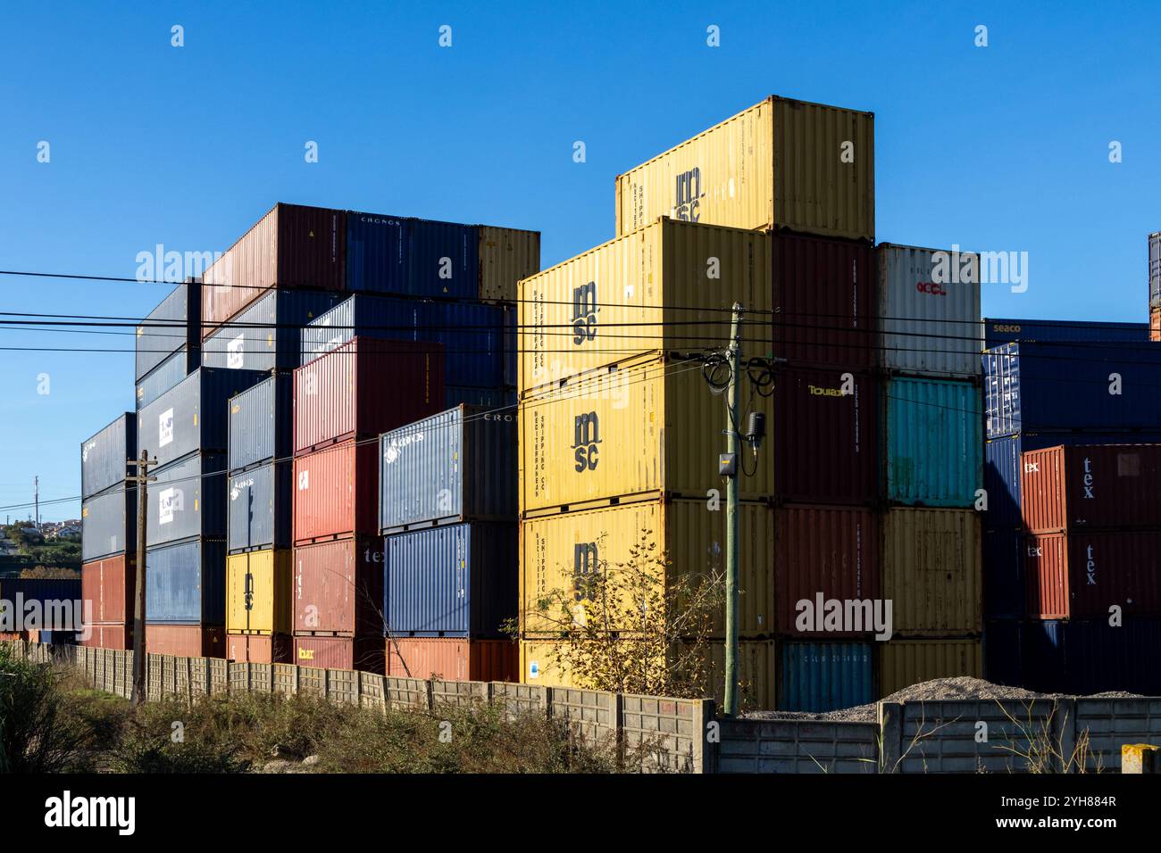 Stacks of colorful intermodal containers behind a concrete wall under a ...