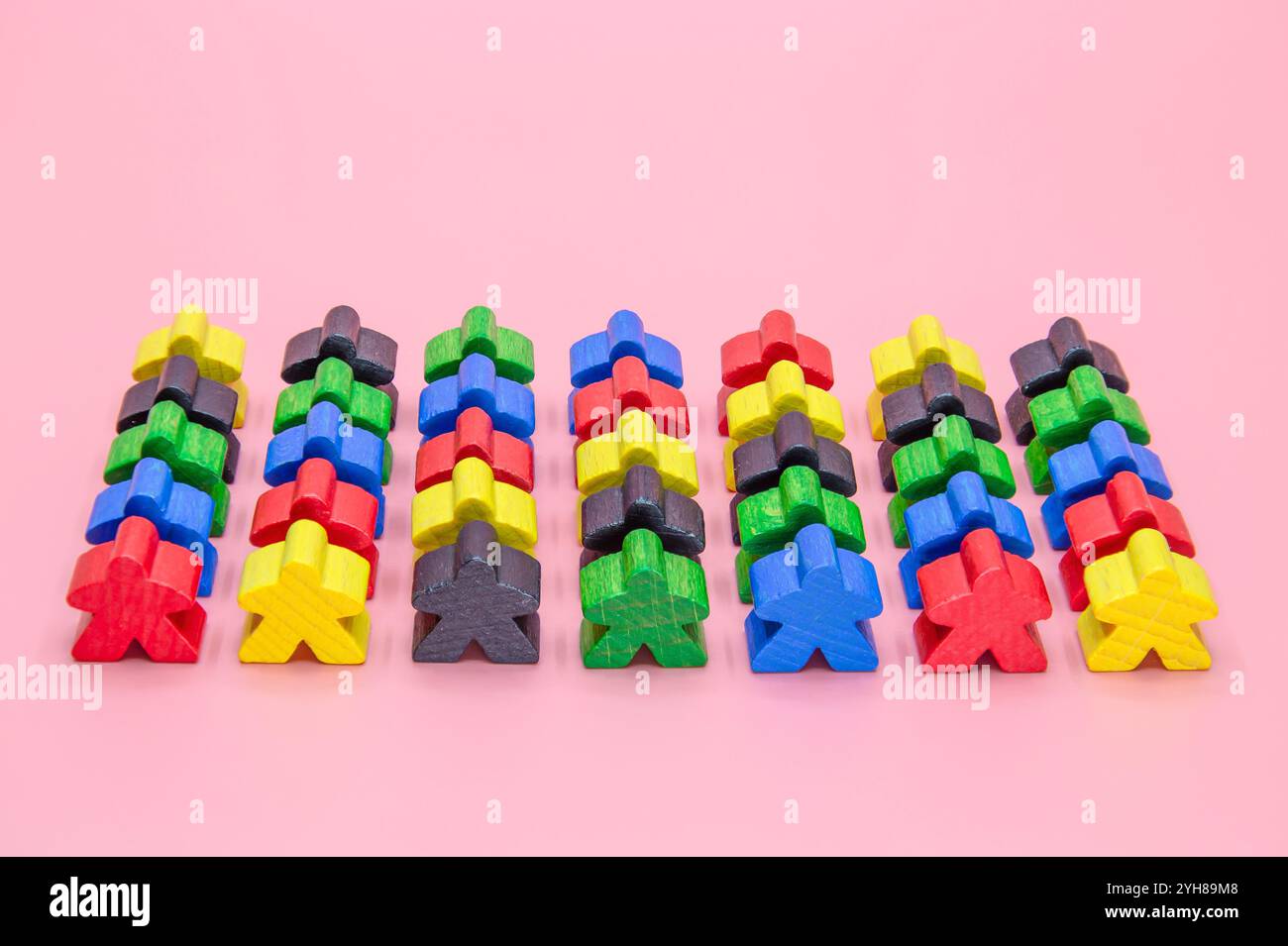 Colorful wooden toy figures of people forming a group on a pink ...