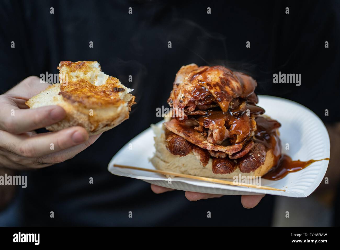 Close up of a person holding a huge sausage and bacon bap, a ...