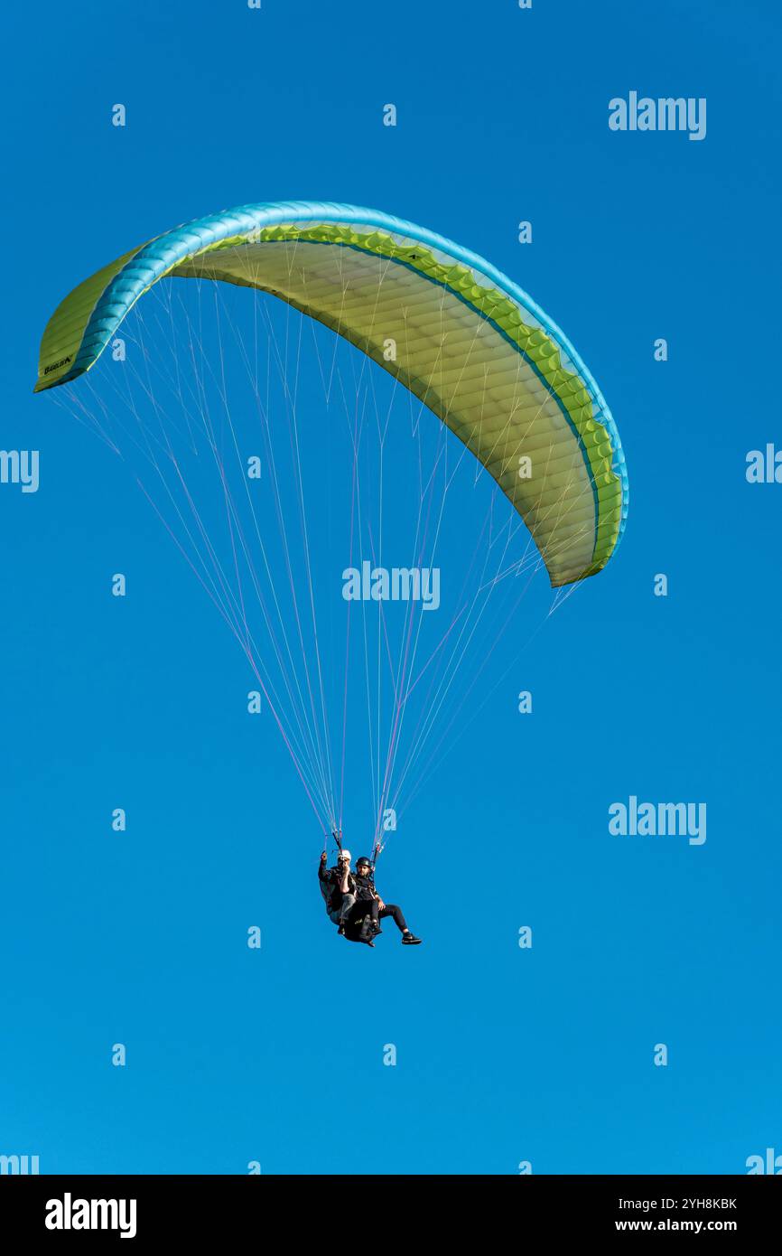 Tandem Paragliders soars high above the landscape under a vibrant ...