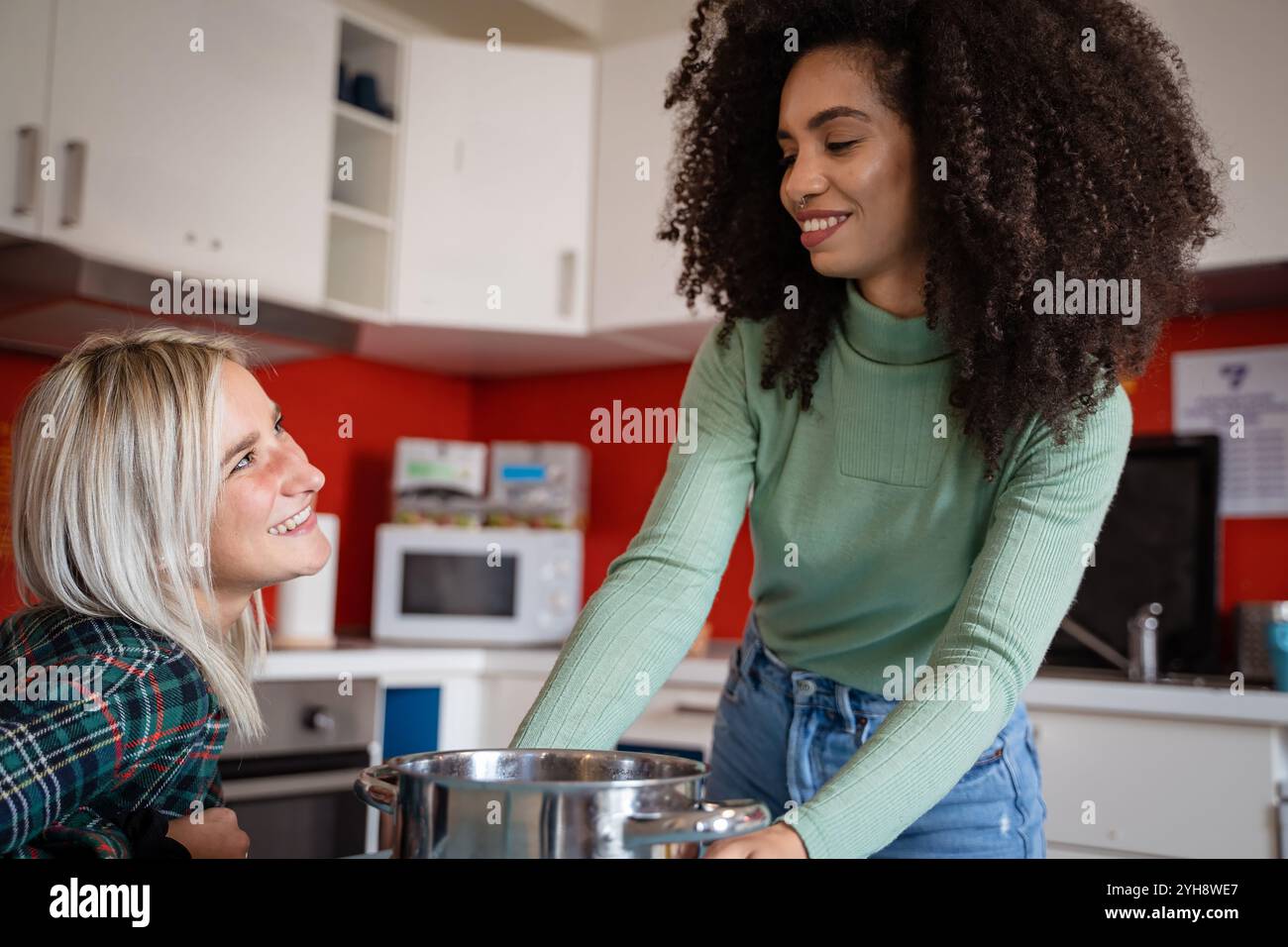 Two diverse young women friends cooking together in modern kitchen ...