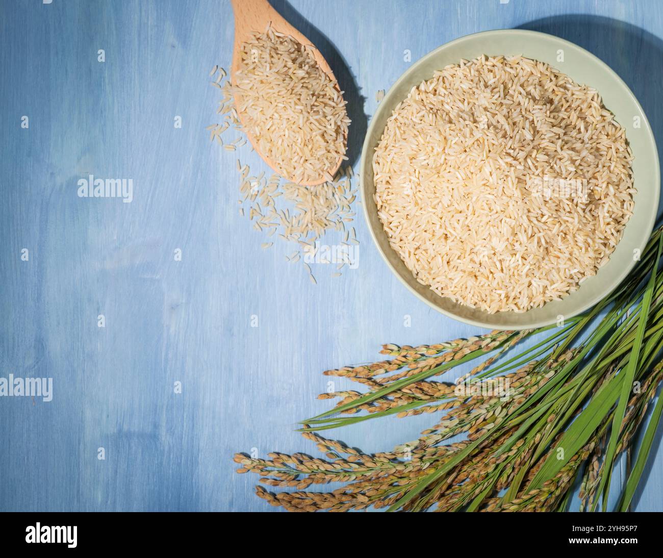 A bowl of brown rice is placed on a blue table next to a spoonful of ...