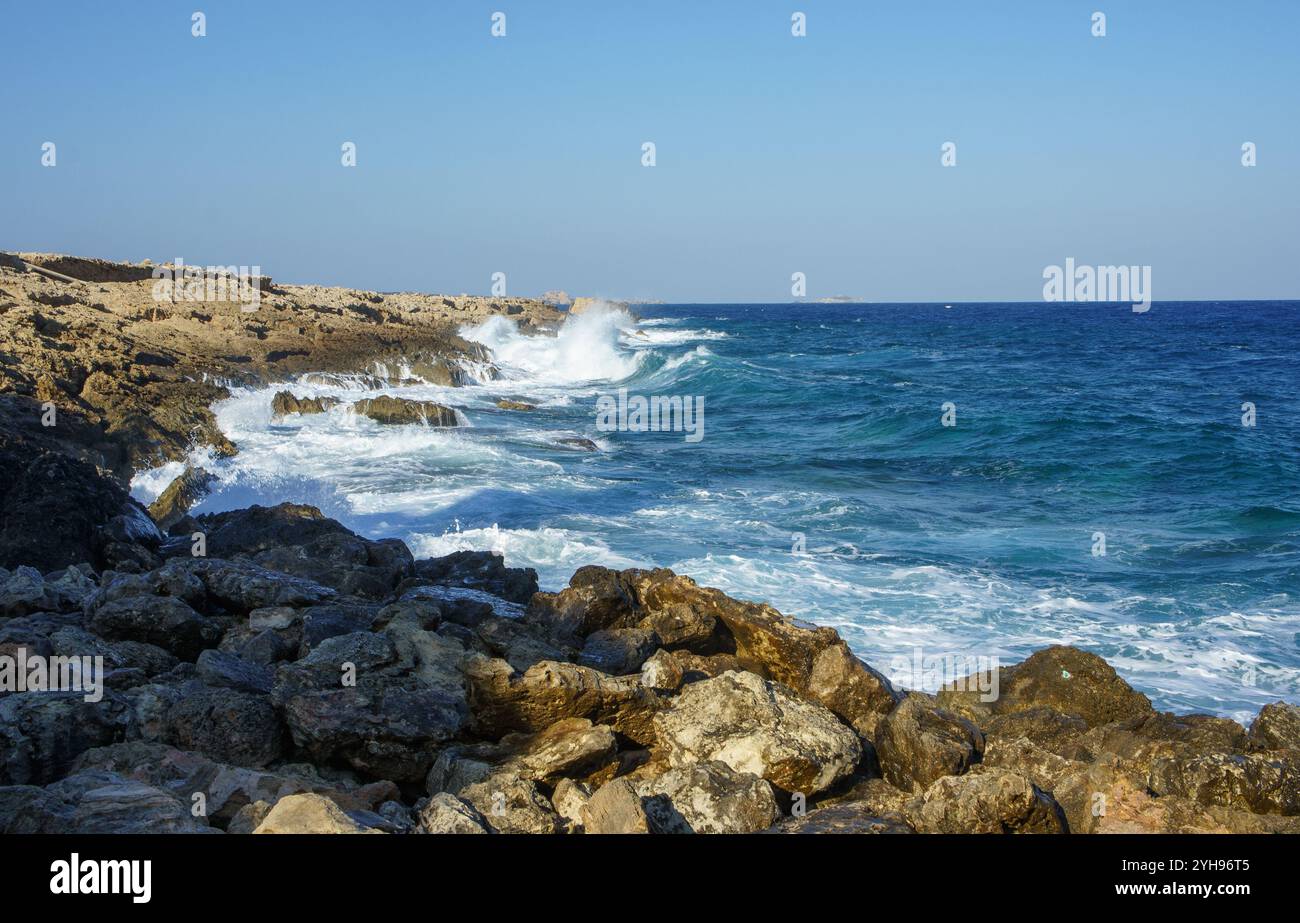 Dynamic waves collide with rugged rocks under a clear blue sky ...