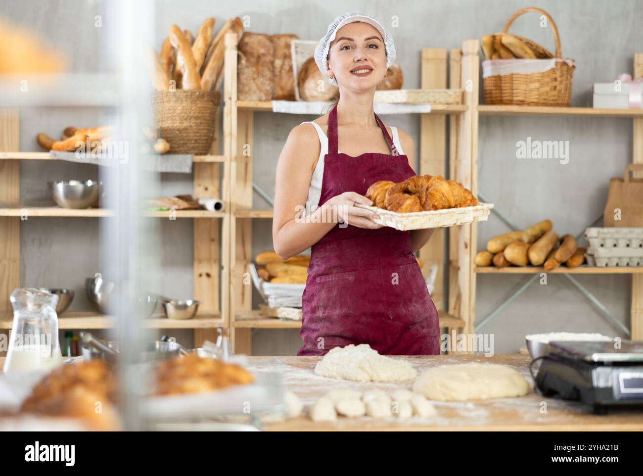 Smiling female baker in white uniform stands behind counter in small ...