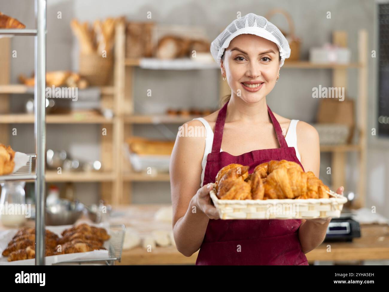 Smiling female baker in white uniform stands behind counter in small ...