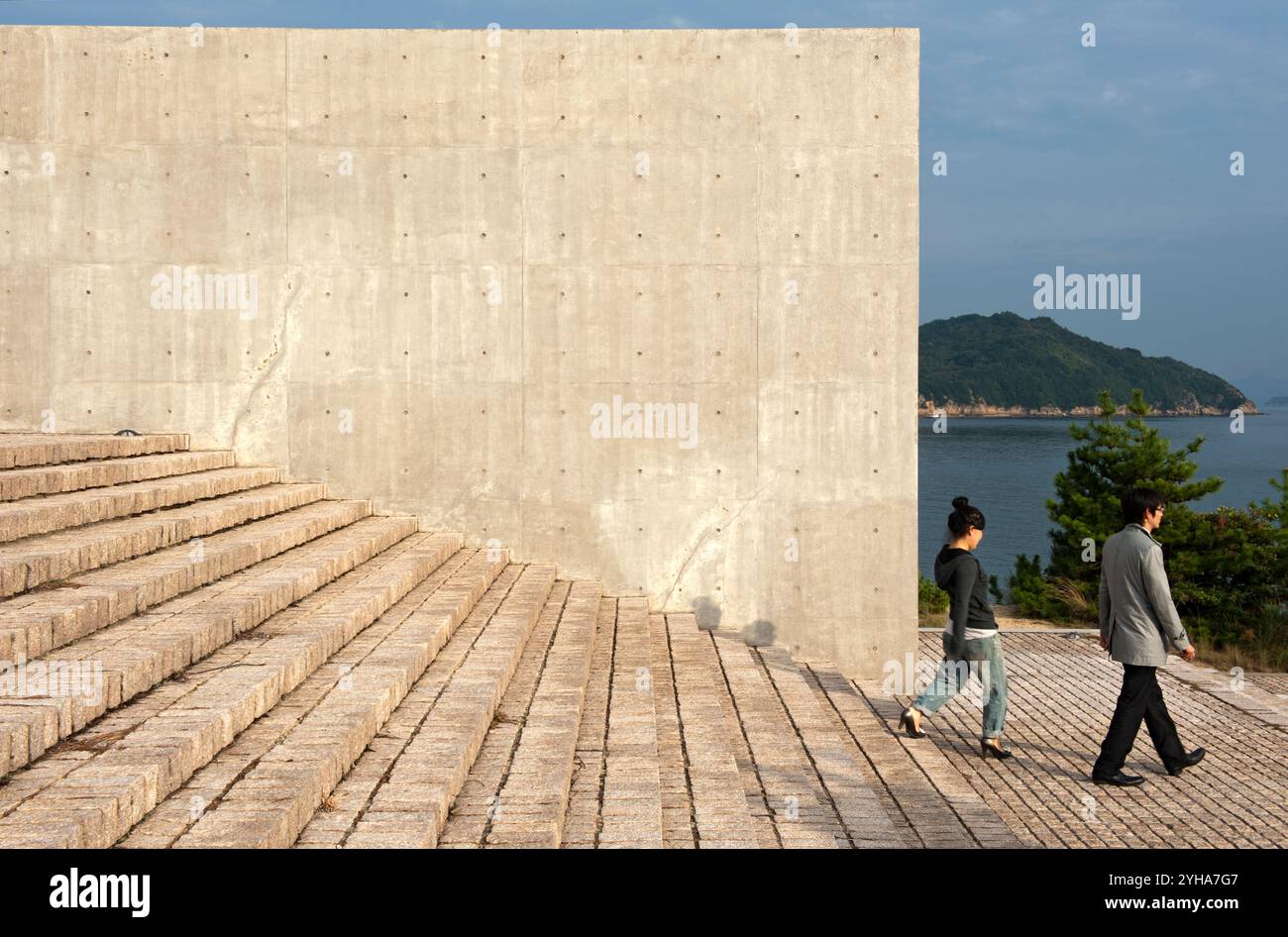 Visitors walking down steps beside an austere concrete wall designed by ...