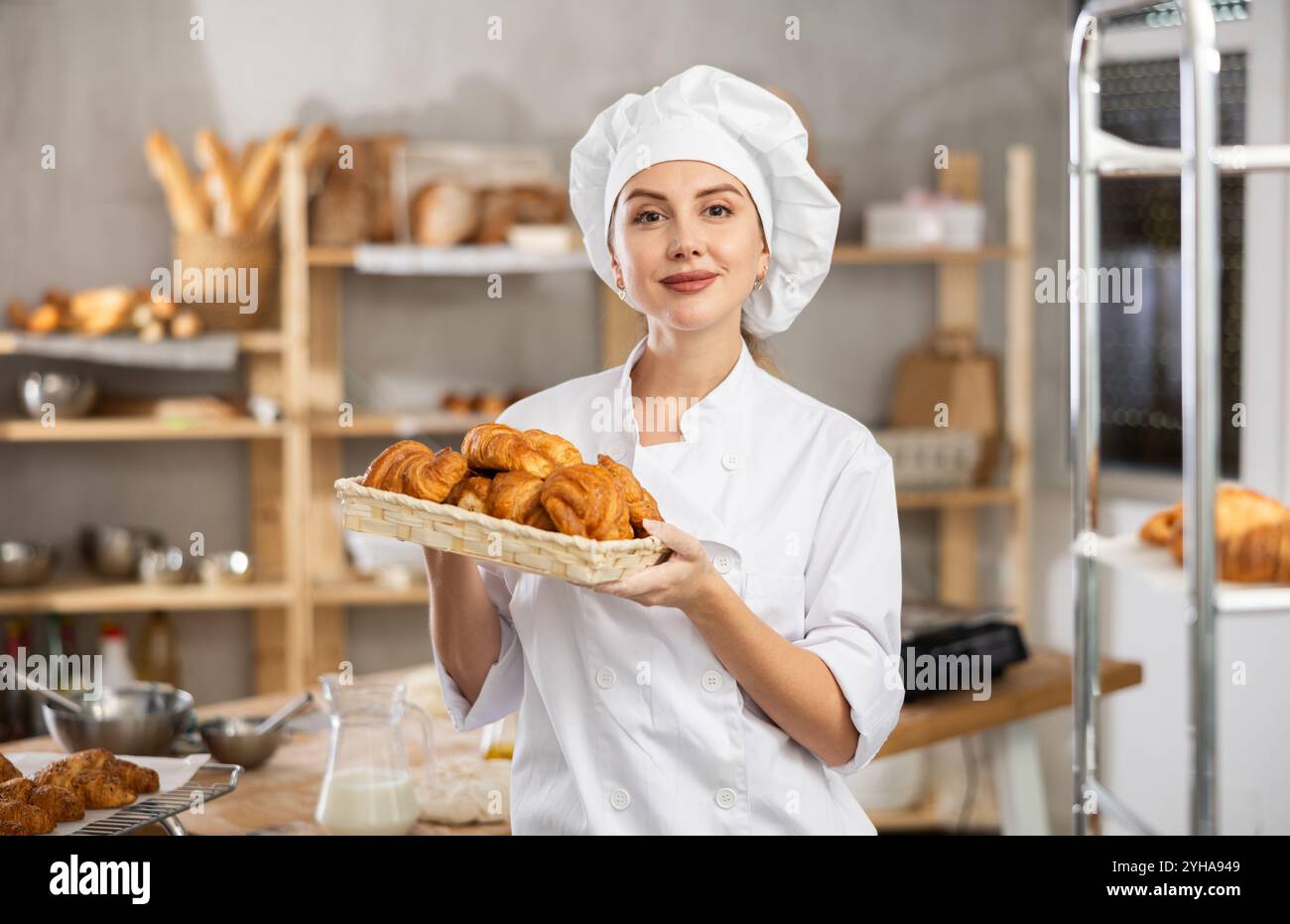 Smiling female baker in white uniform stands behind counter in small ...