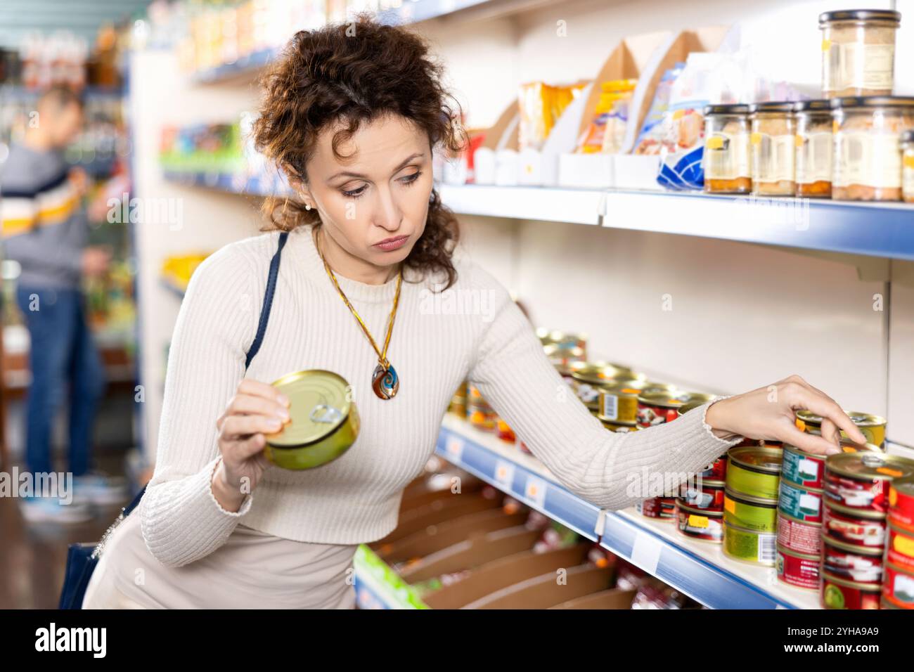 Female shopper chooses canned fish in grocery store. Woman shopper ...