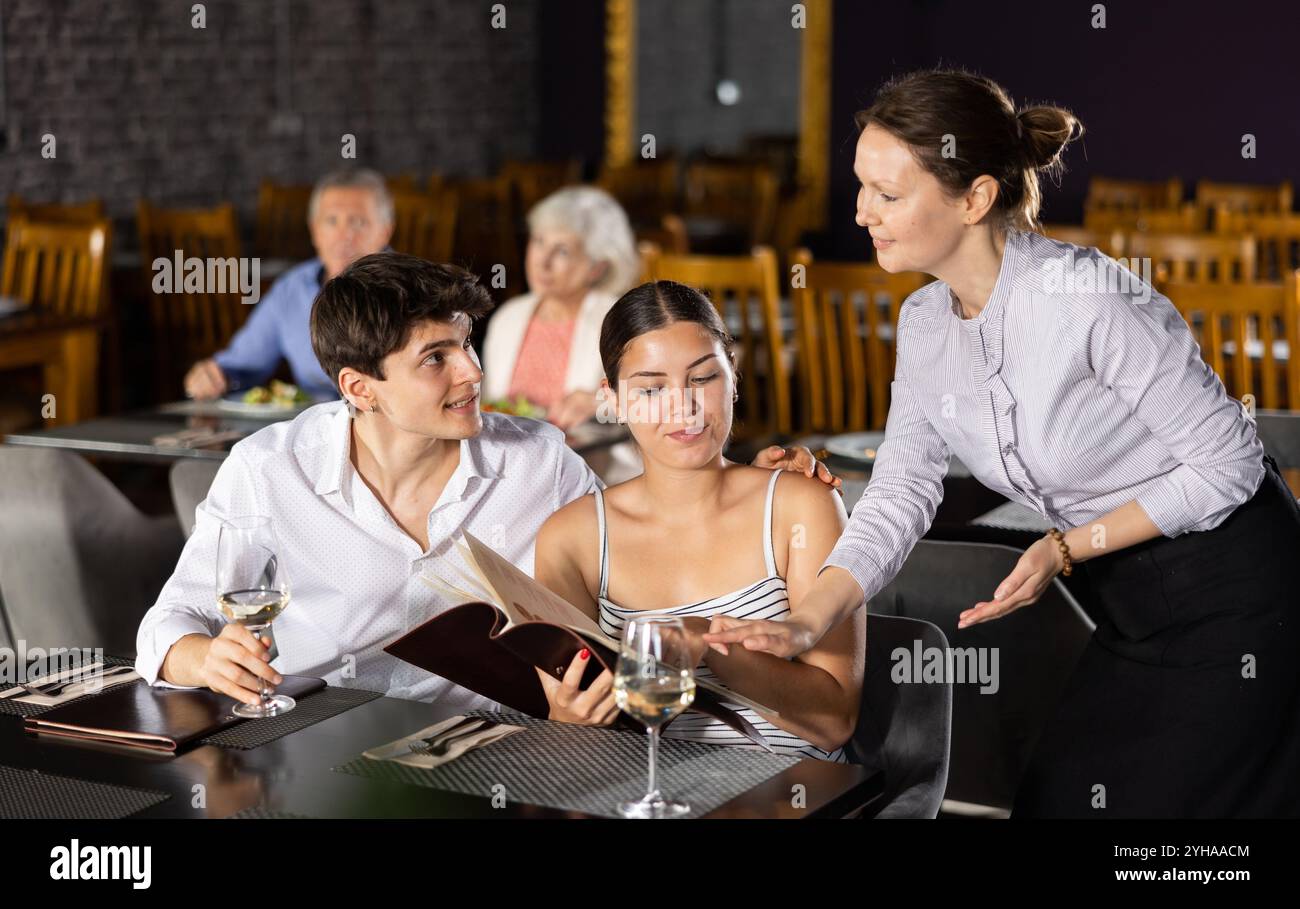 Young couple discussing menu with waitress at table in restaurant Stock ...