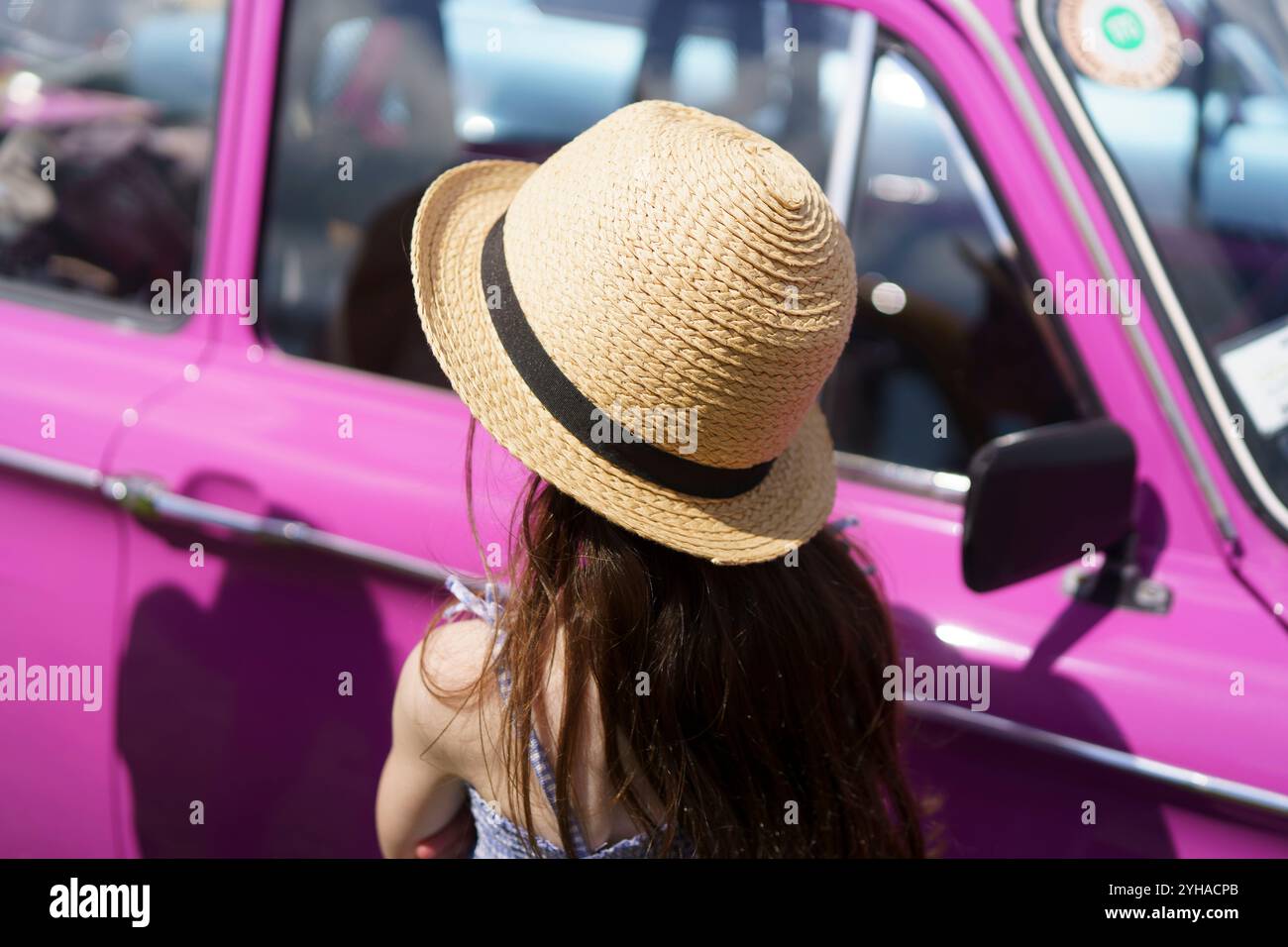 A cute little girl in a sundress and a straw hat stands with her back ...