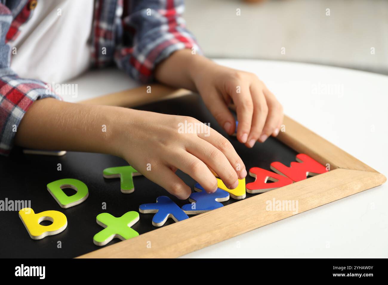 Little boy learning alphabet with magnetic letters at white table ...