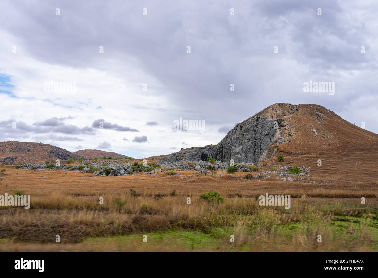 A rugged hill with rocky outcrops under a cloudy sky. Dry grassland ...