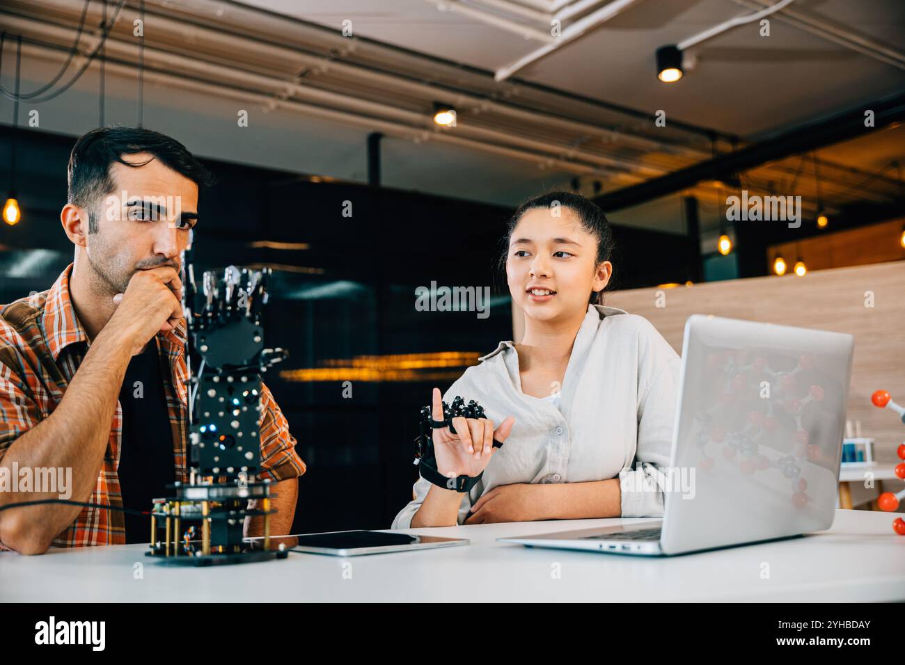 Teacher aids student working on a robotic arm in classroom design and ...