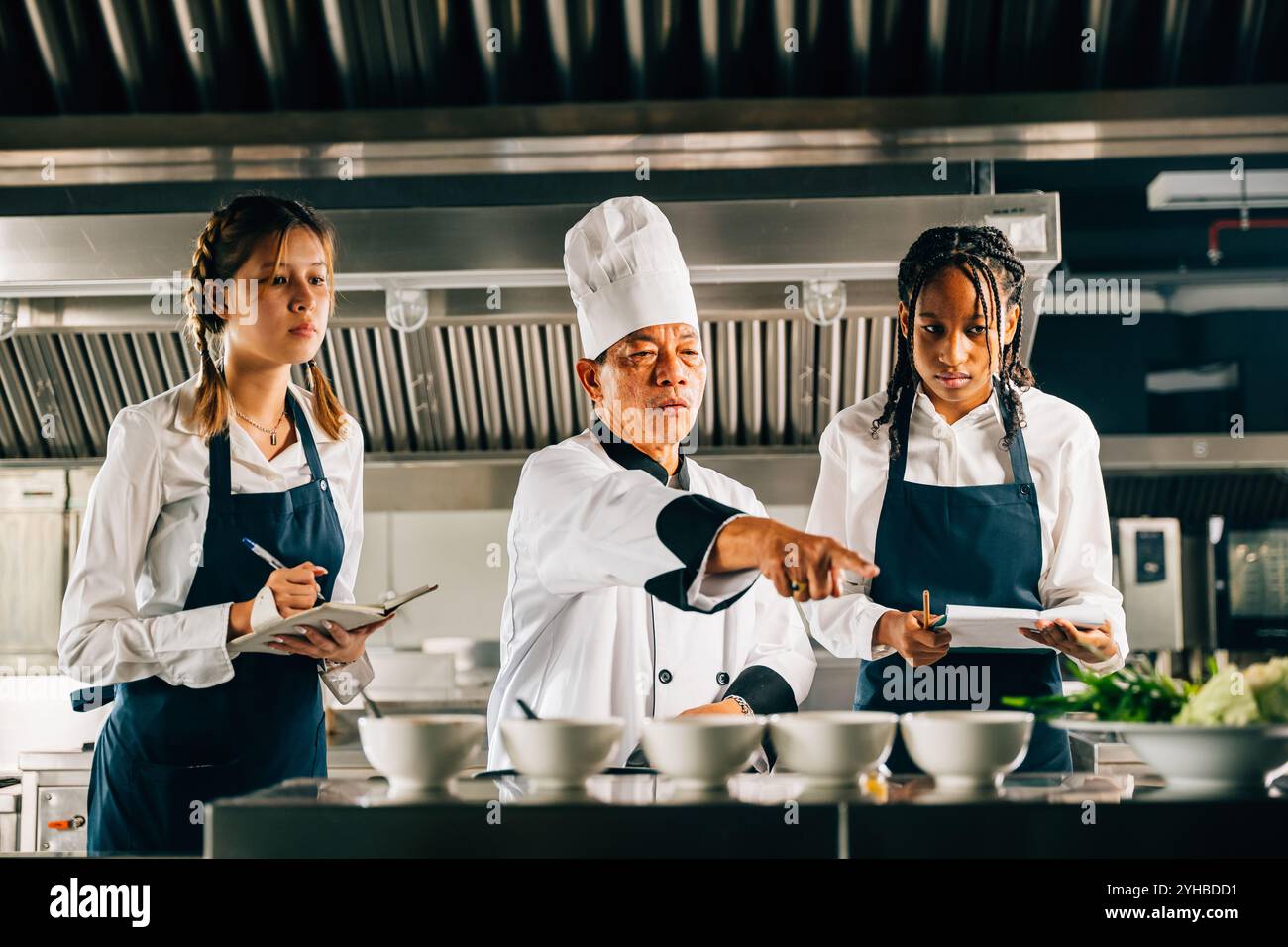 In a restaurant kitchen a senior Asian chef educates multiracial ...