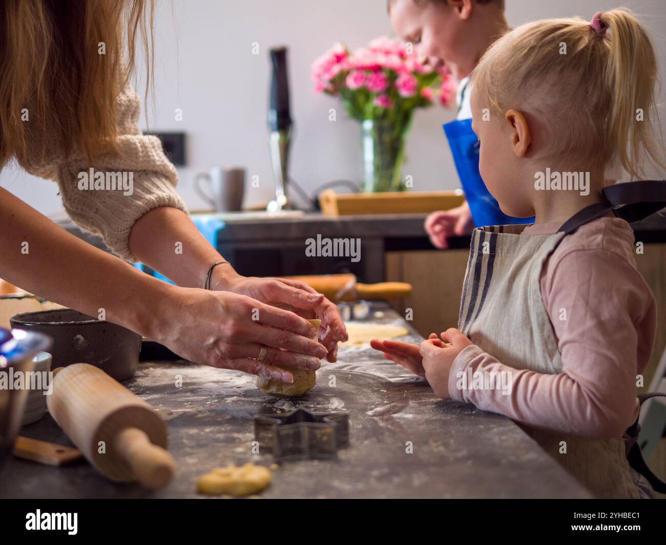 Mother and kids make cookies in lively kitchen, with dough taking shape ...