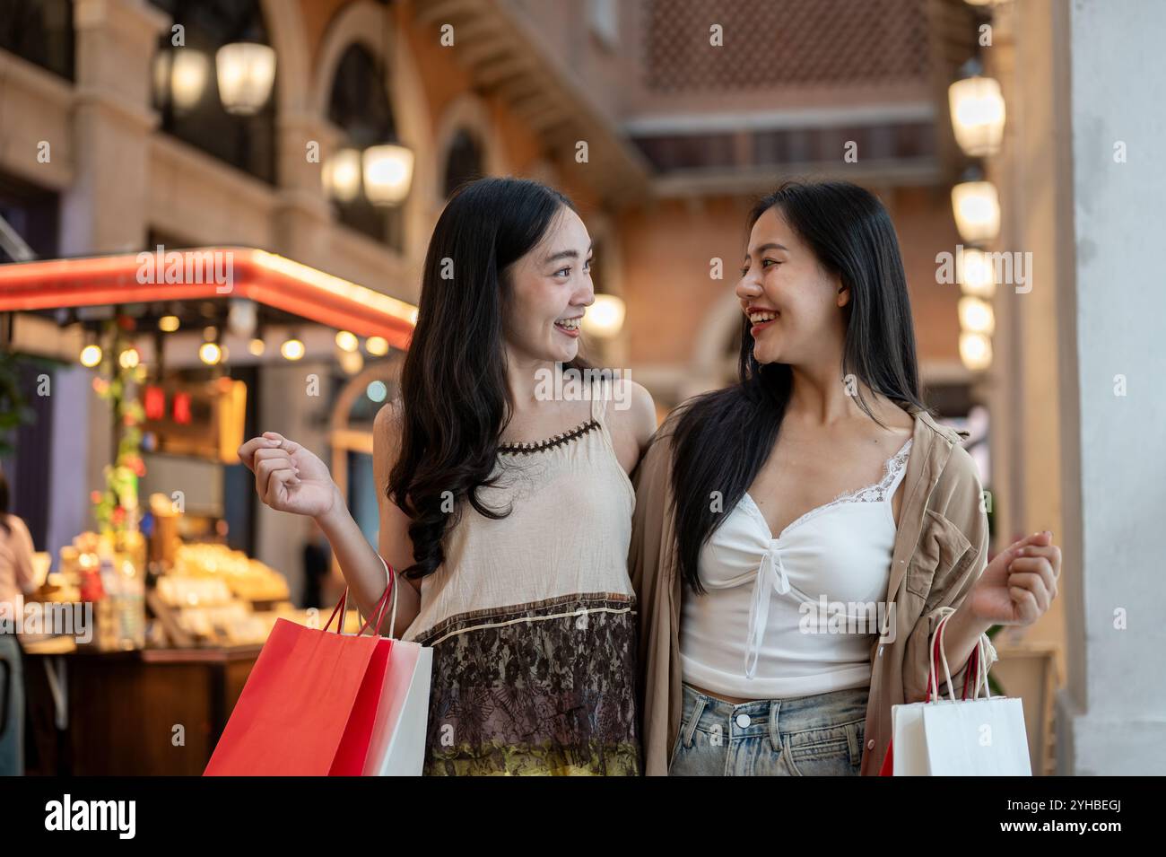Two charming and smiling Asian female friends enjoy shopping together ...