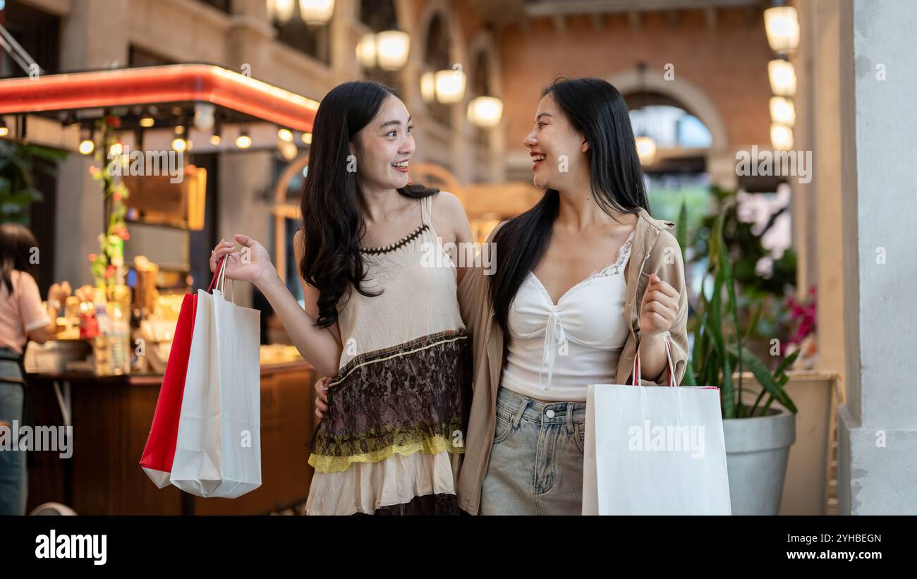 Two charming and smiling Asian female friends enjoy shopping together ...