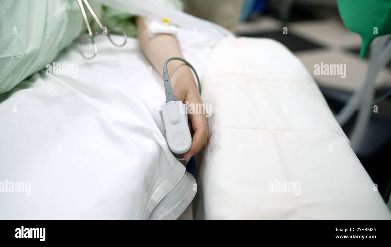 Close-up of a patient's hand resting on a hospital bed with a pulse ...