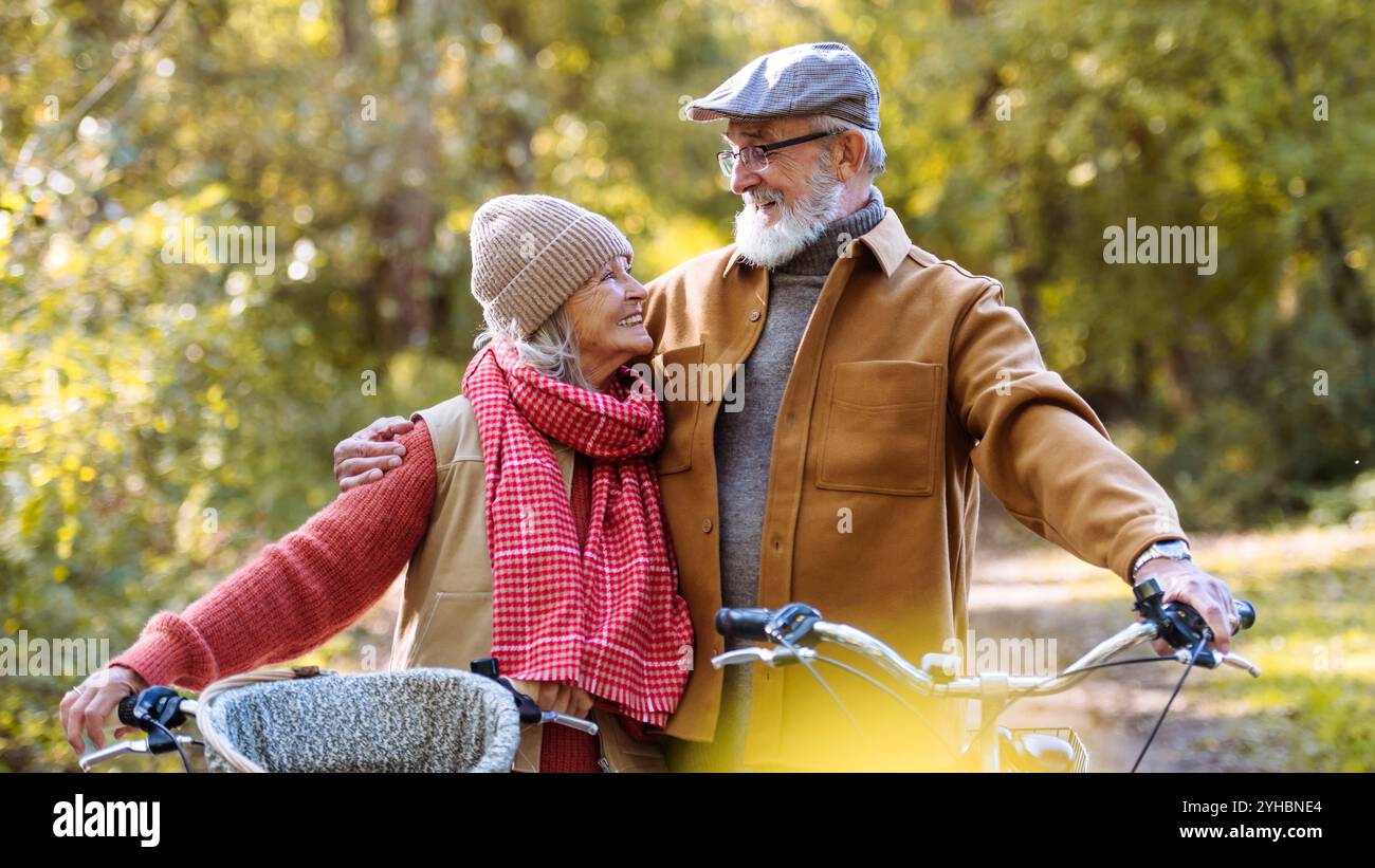 Lovely elderly couple on a walk in the forest, pushing their bikes side ...