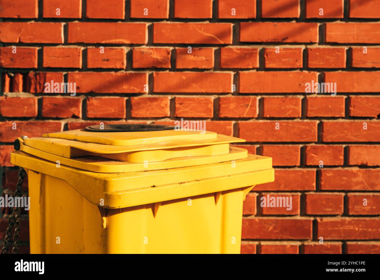 Yellow plastic trash bin against brick wall, selective focus Stock Photo - Alamy