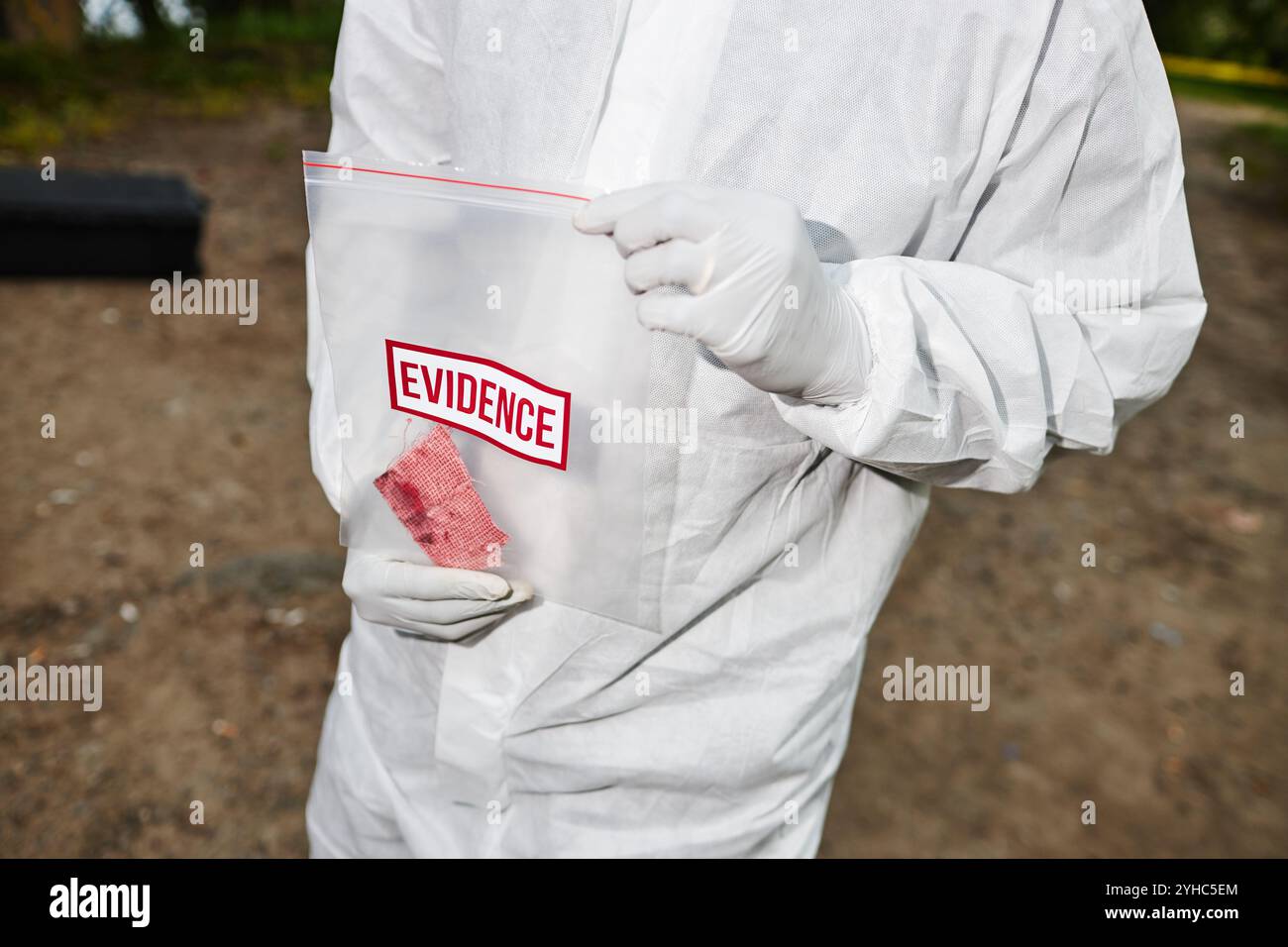 Closeup of man wearing protective suit holding plastic bag marked Evidence while working on ...