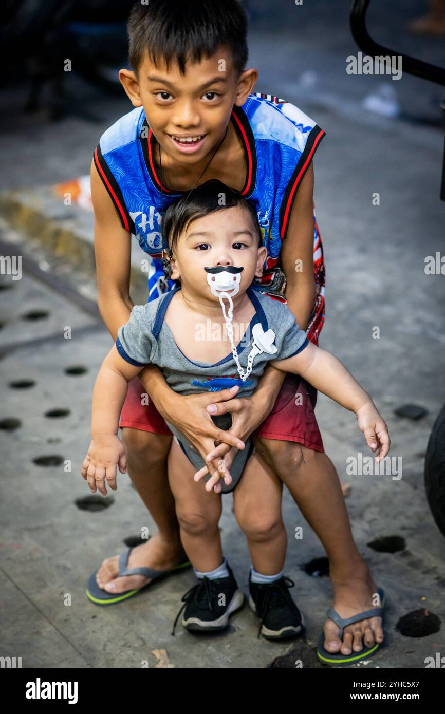 A young filipino boy plays with a baby, possibly his younger brother in ...