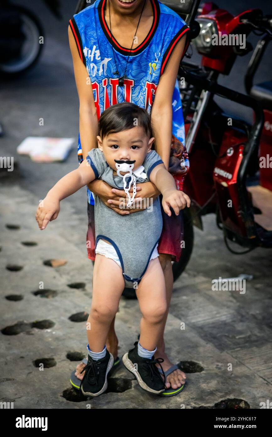 A young filipino boy plays with a baby, possibly his younger brother in ...