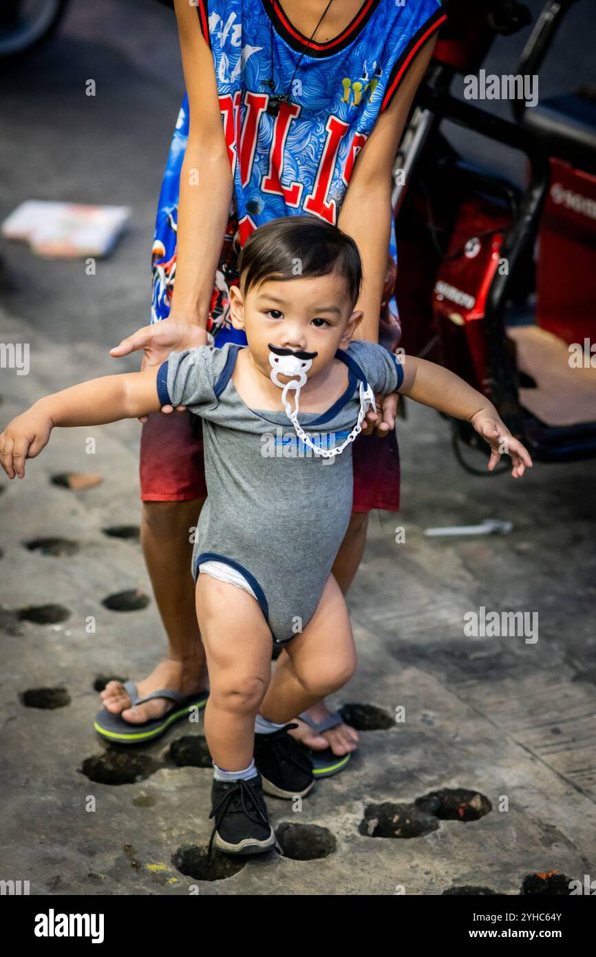 A young filipino boy plays with a baby, possibly his younger brother in ...