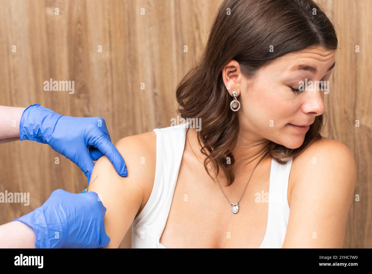 Woman afraid of syringe injection turning away as medical assistant in gloves administers an ...