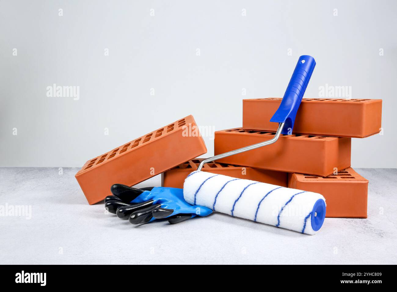 Red bricks, paint roller and gloves on textured table against light ...