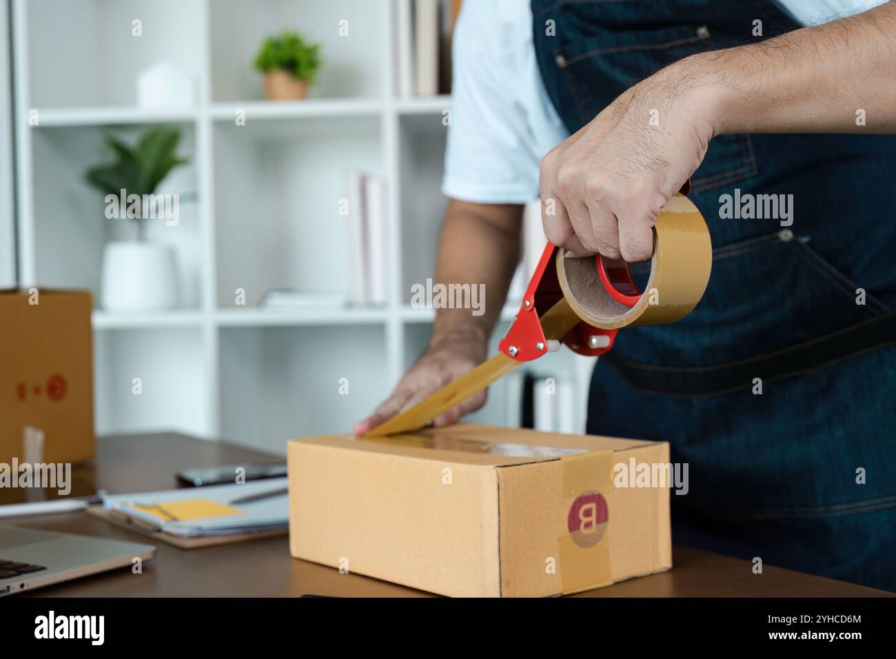 Man Sealing Cardboard Box with Tape in Home Office Setting for E ...