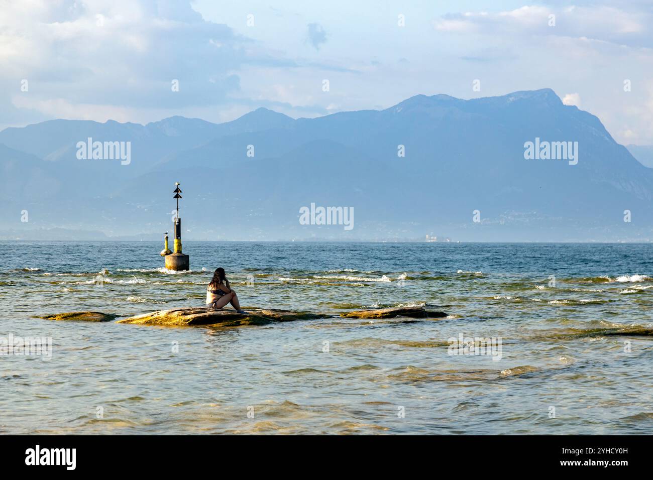 Sirmione, Italy - Sep 21st, 2024: A woman relaxes on lakeside rocks ...
