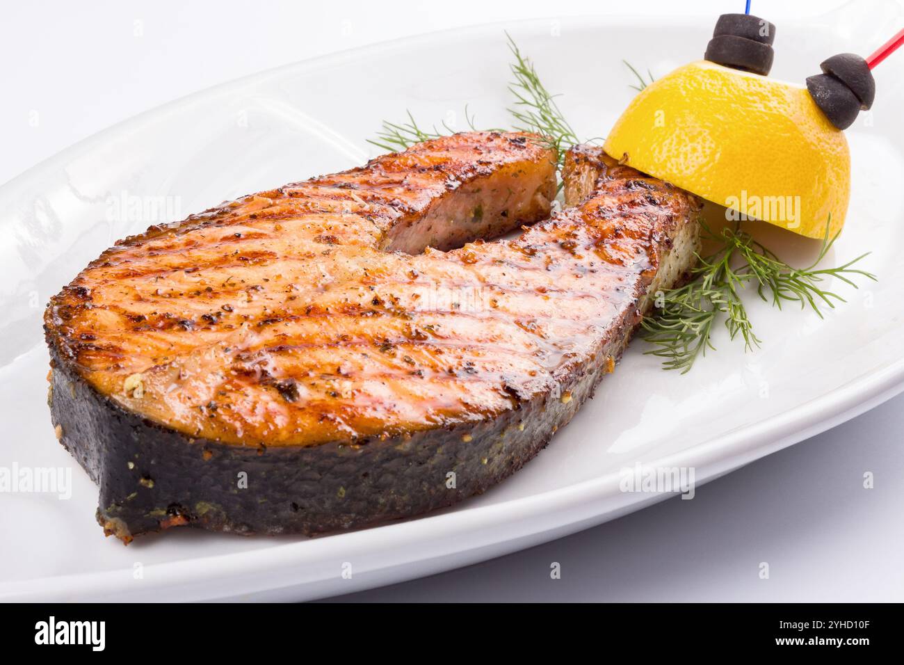 grilled fish steak on the white plate decorated with lemon. closeup ...