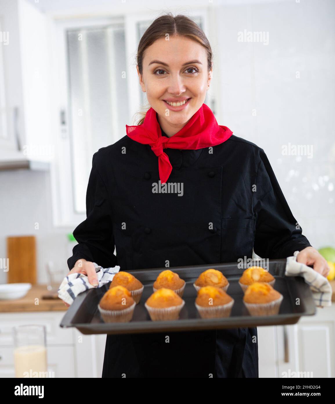 Smiling female chef in black uniform standing in private kitchen with ...