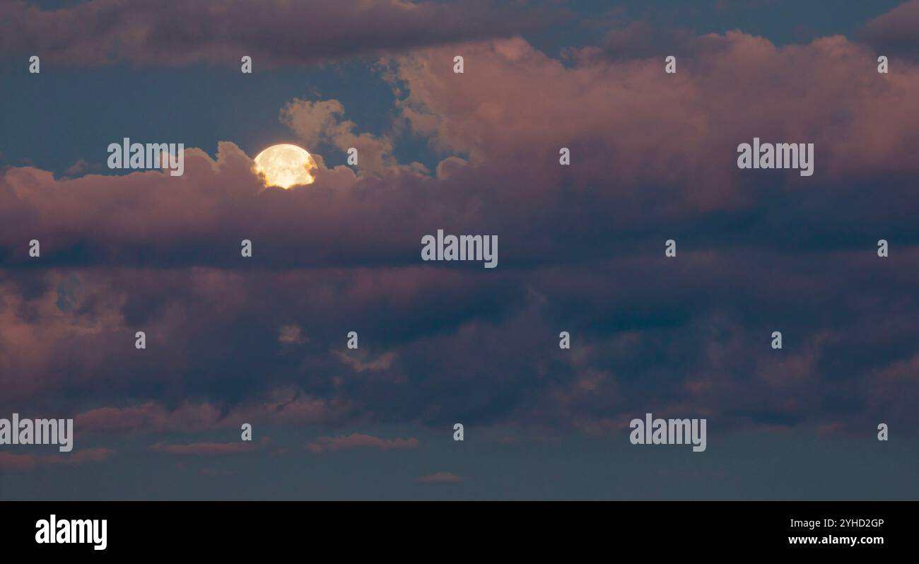 Full moon rising beind the clouds that still have color in them after ...