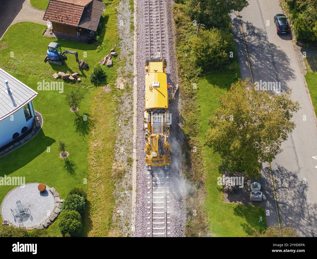 Yellow train runs along the railway tracks through the village next to ...