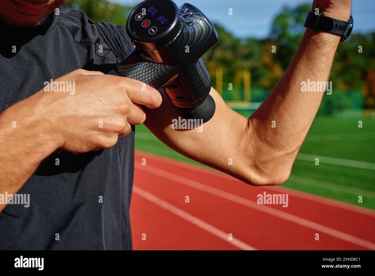 Close-up of male athlete using handheld massage gun on arm muscles for ...
