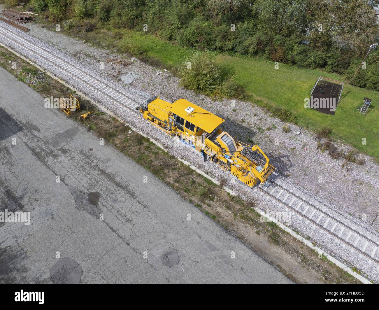 A yellow construction machine working on railway tracks near a road and ...