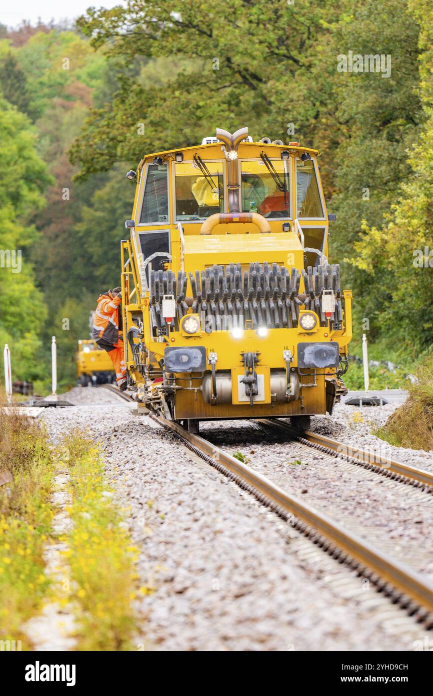 Yellow tractor moving on a railway track through a densely wooded area ...
