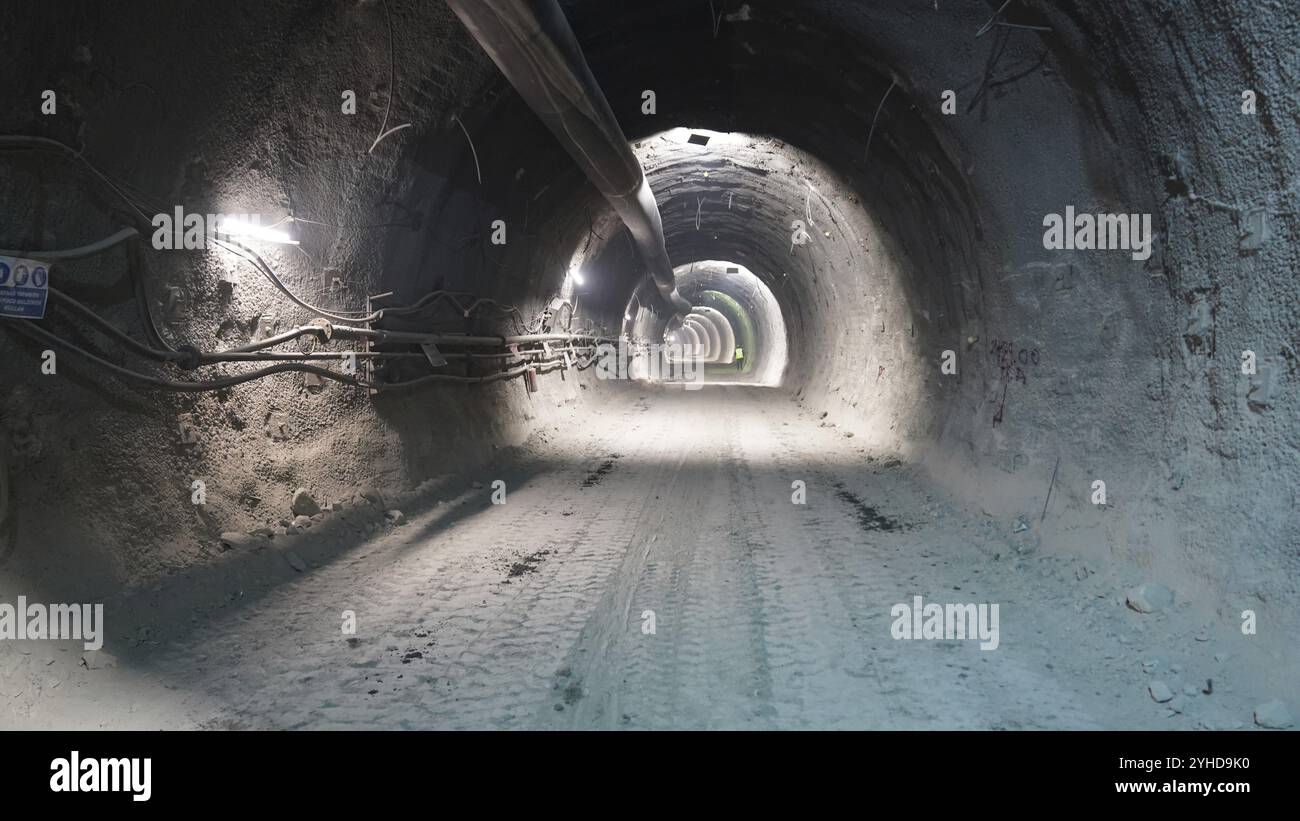 A dimly lit underground tunnel with pipes along the walls and a sandy ...