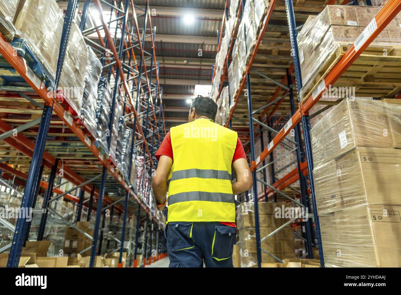 Rear view of a male worker walking along boxes in storage warehouse ...