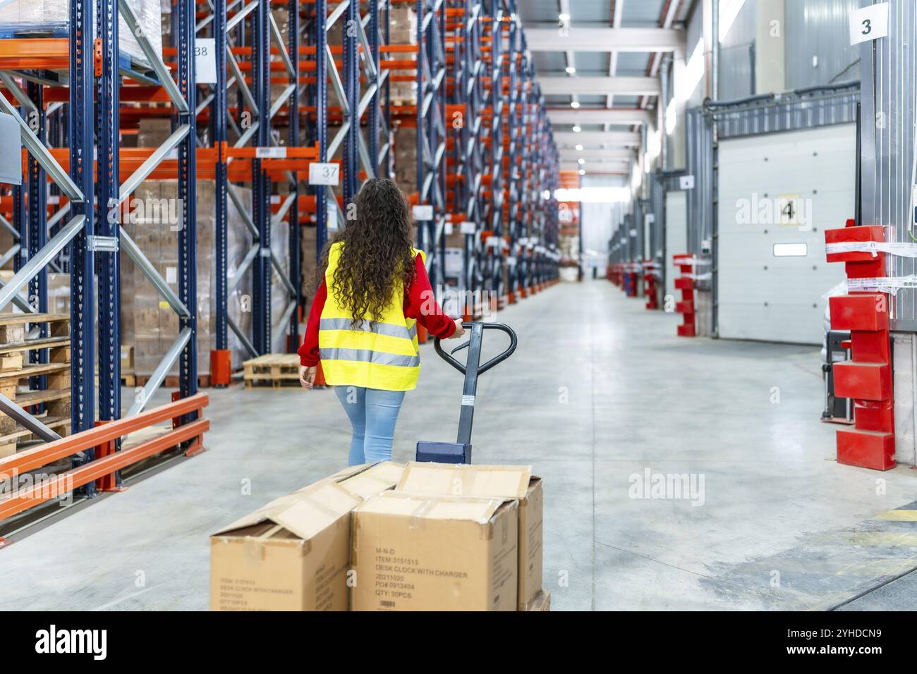 Rear view of a woman carrying trolley with boxes along a corridor of a ...