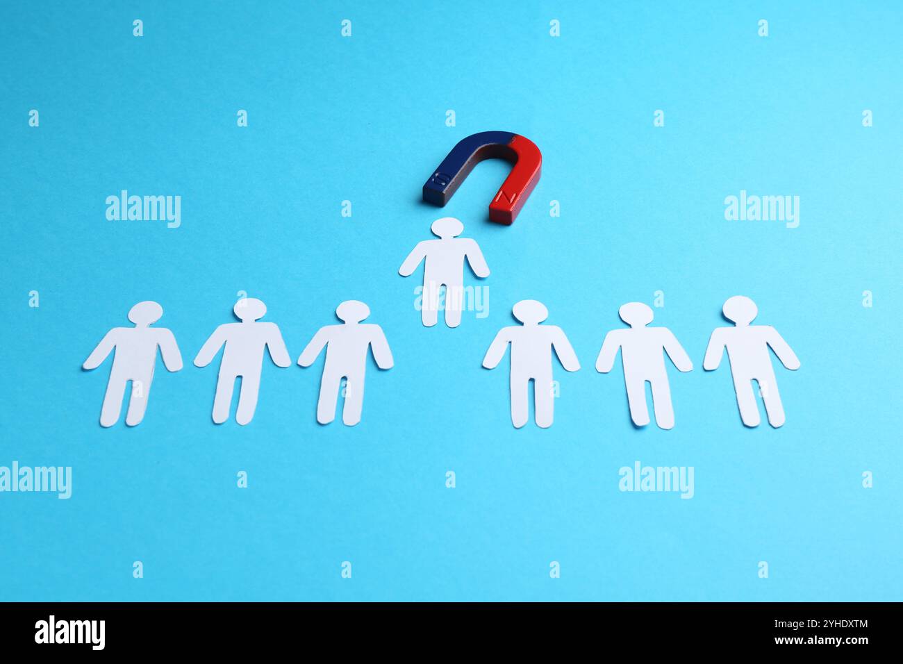 Magnet attracting paper cutouts of humans on light blue background ...