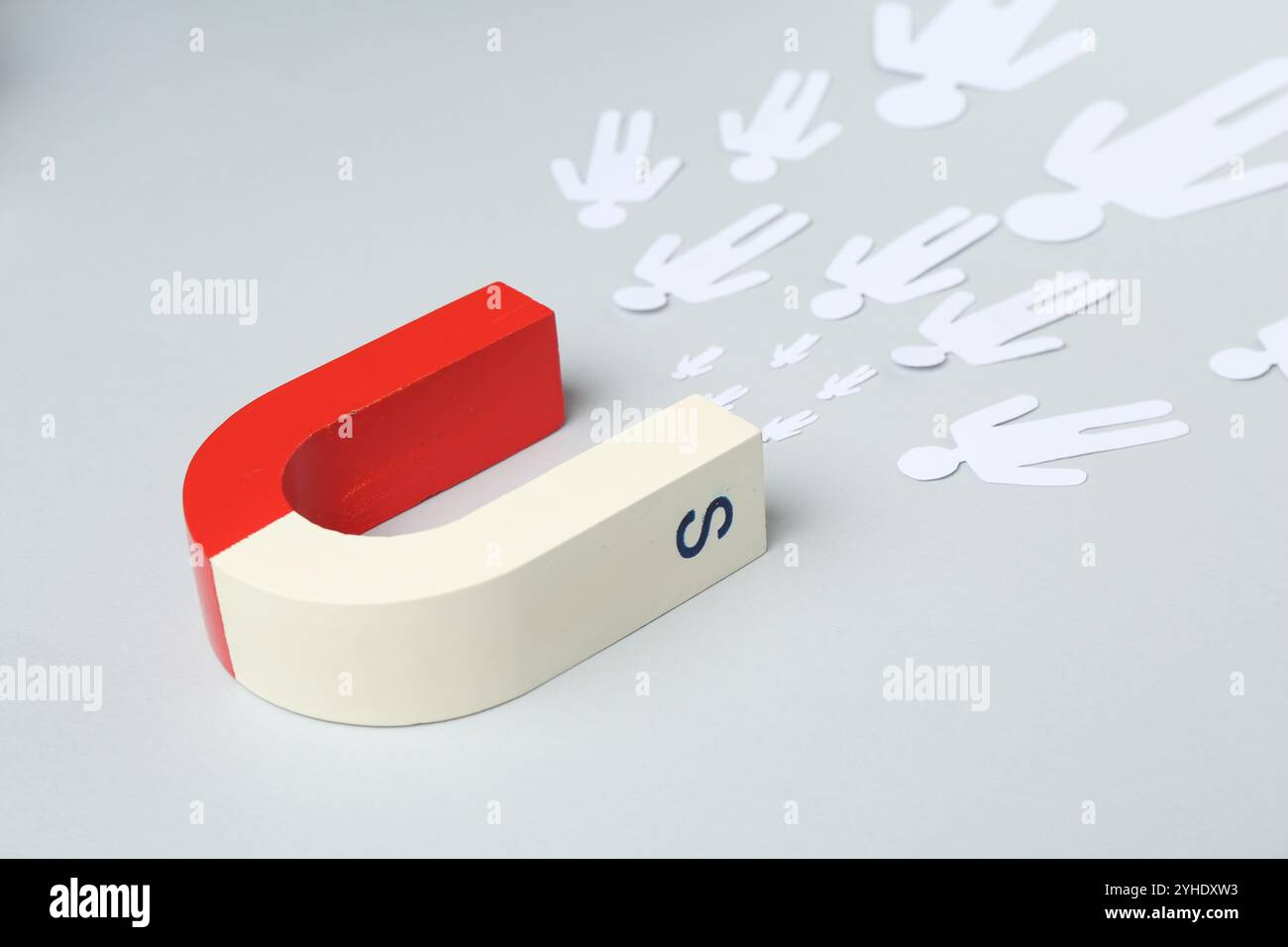 Magnet attracting paper cutouts of humans on light grey background ...