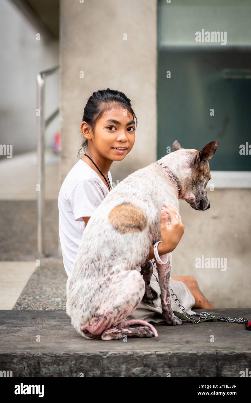 A beautiful young Filipino girl poses and smiles holding her pet dog ...