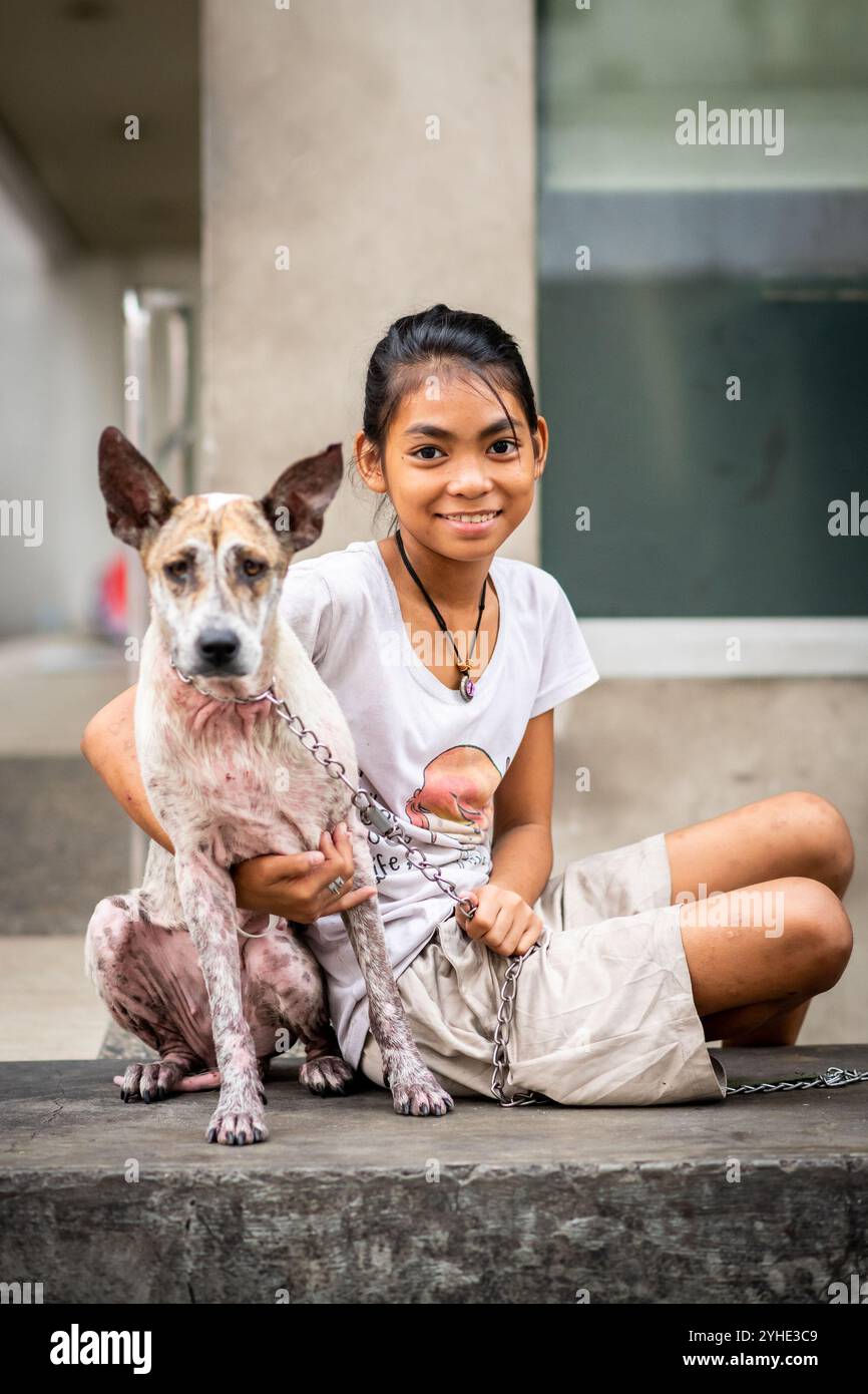 A beautiful young Filipino girl poses and smiles holding her pet dog ...