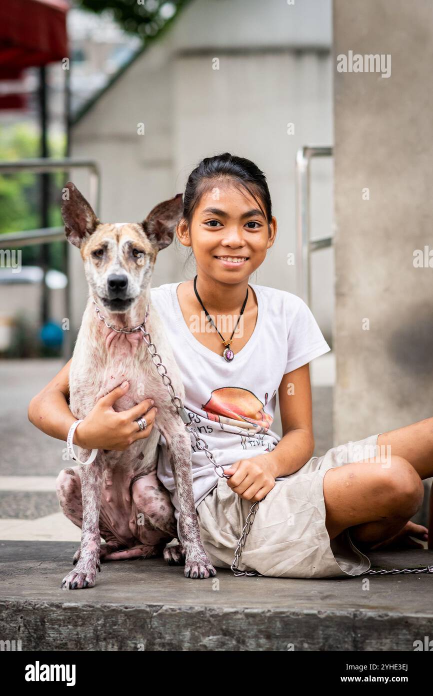 A beautiful young Filipino girl poses and smiles holding her pet dog ...