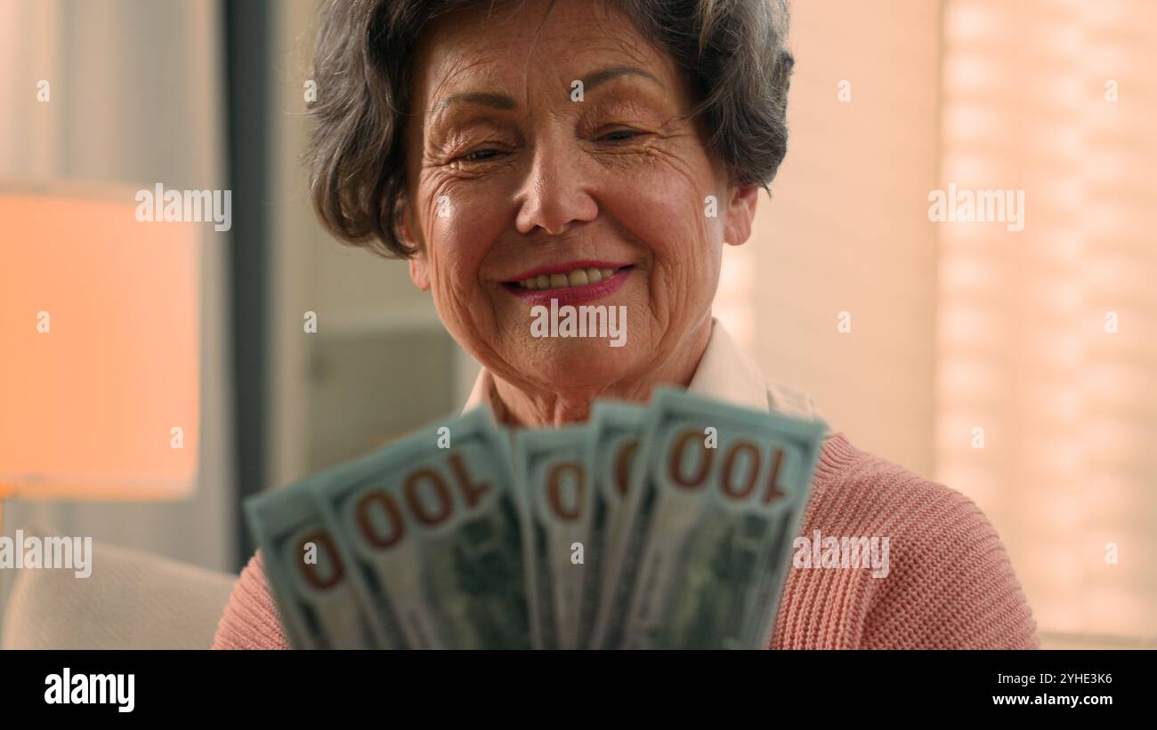 Happy smiling rich Caucasian old woman count money at home bills ...