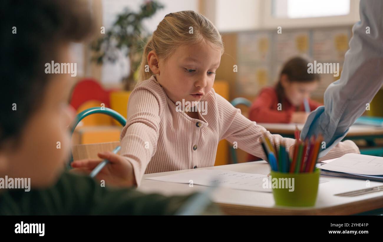 Caucasian woman teacher in elementary school teach children class kids writing task in classroom ...